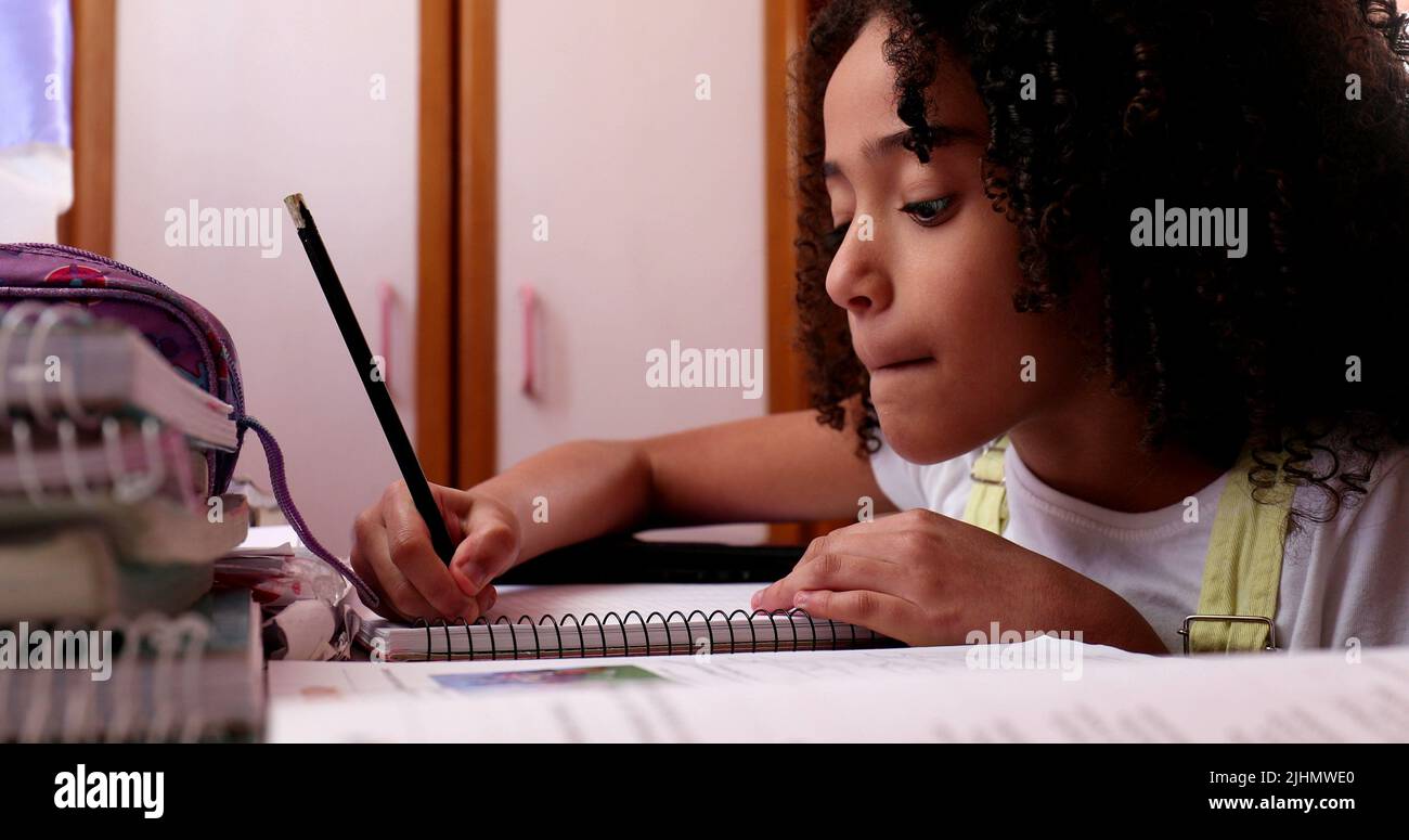 Little girl studying at home, mixed race child writing notes doing ...