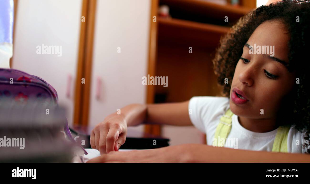 Little girl studying at home, mixed race child writing notes doing ...