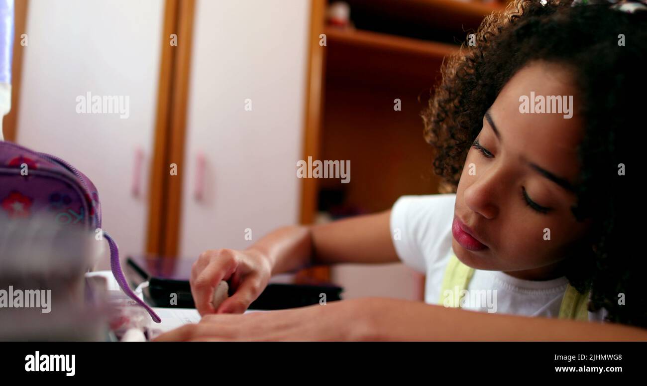 Little girl studying at home, mixed race child writing notes doing ...