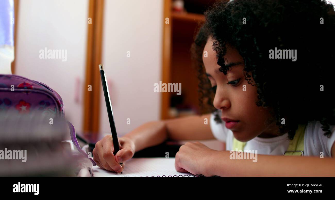 Little girl studying at home, mixed race child writing notes doing ...