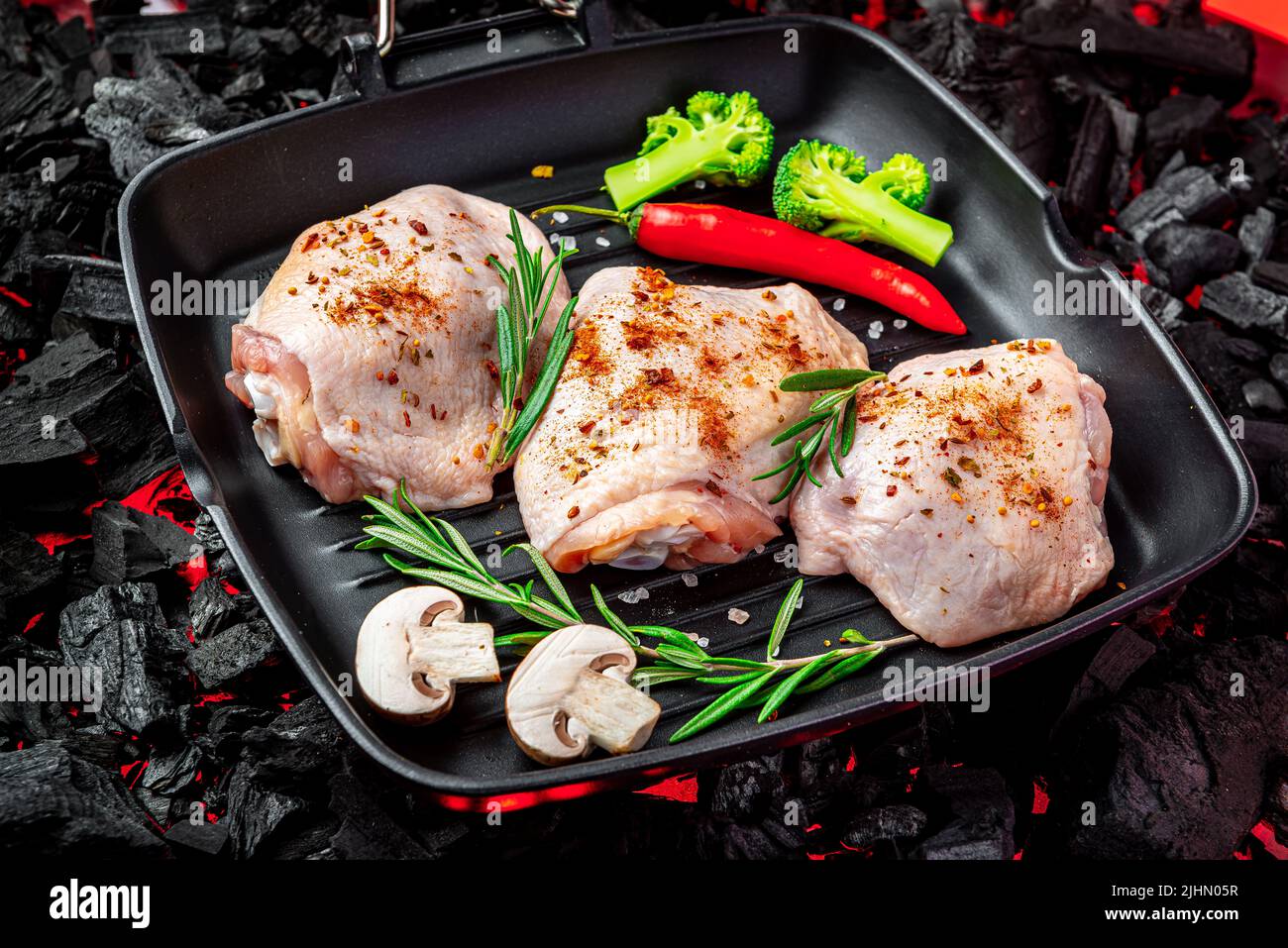 Raw chicken thighs in a pan with vegetables and spices stand on a hot ...