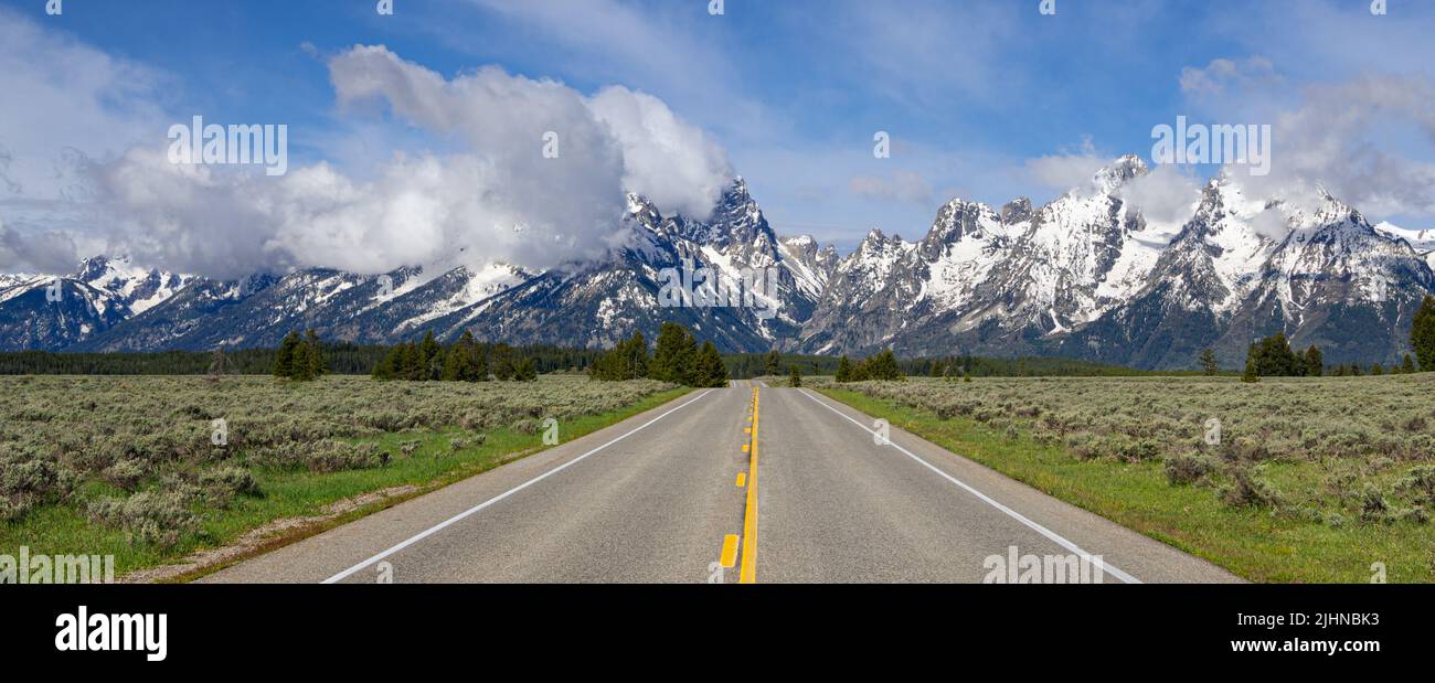 Panorama of a highway into a mountain range of snow-capped peaks under ...