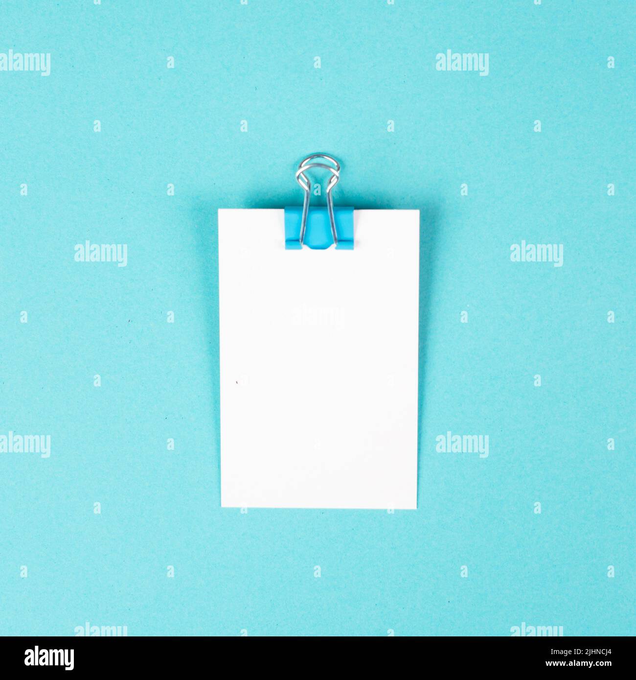 Blank white paper with a paperclip on a blue colored background, copy ...