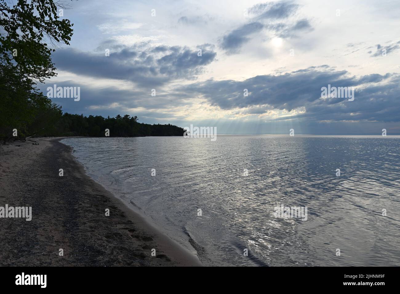 The sun streaks through the clouds on a calm day at the Apostle Islands ...