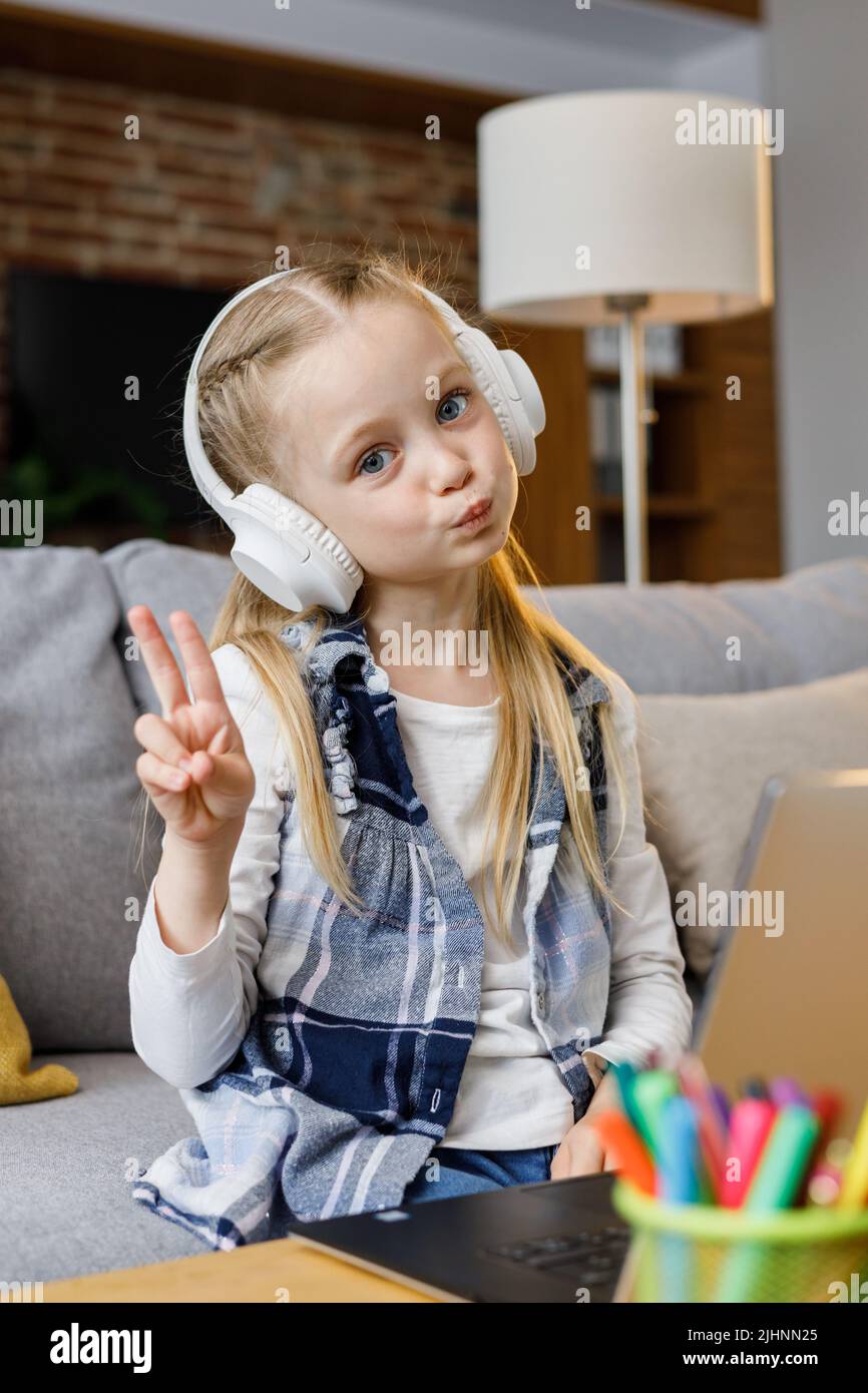 Portrait of cute primary school girl studying at home using laptop ...
