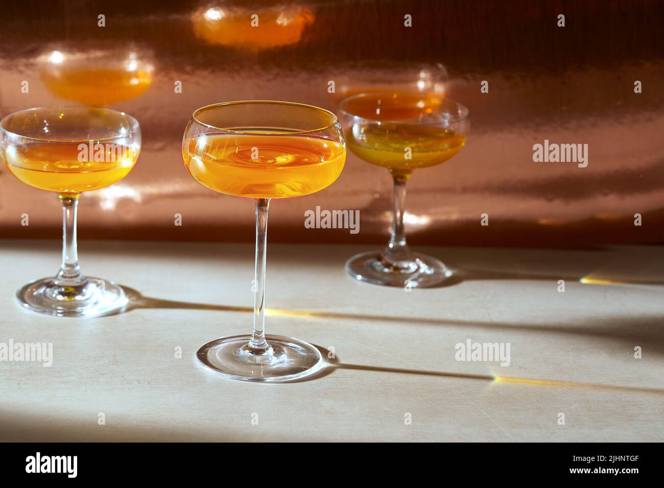 Three cocktail glassed with copper orange drinks on neutral table with ...