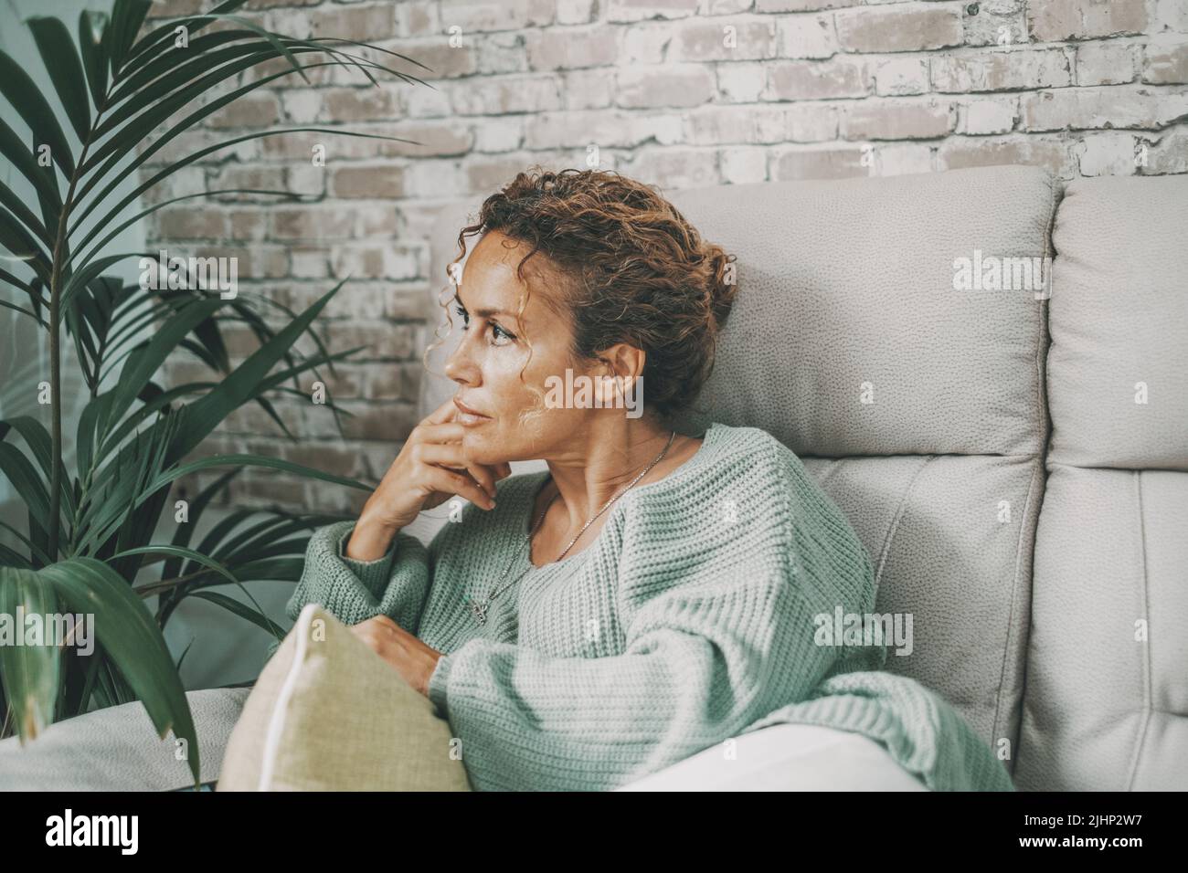Thoughtful and worried lady at home sitting on the sofa looking serious ...