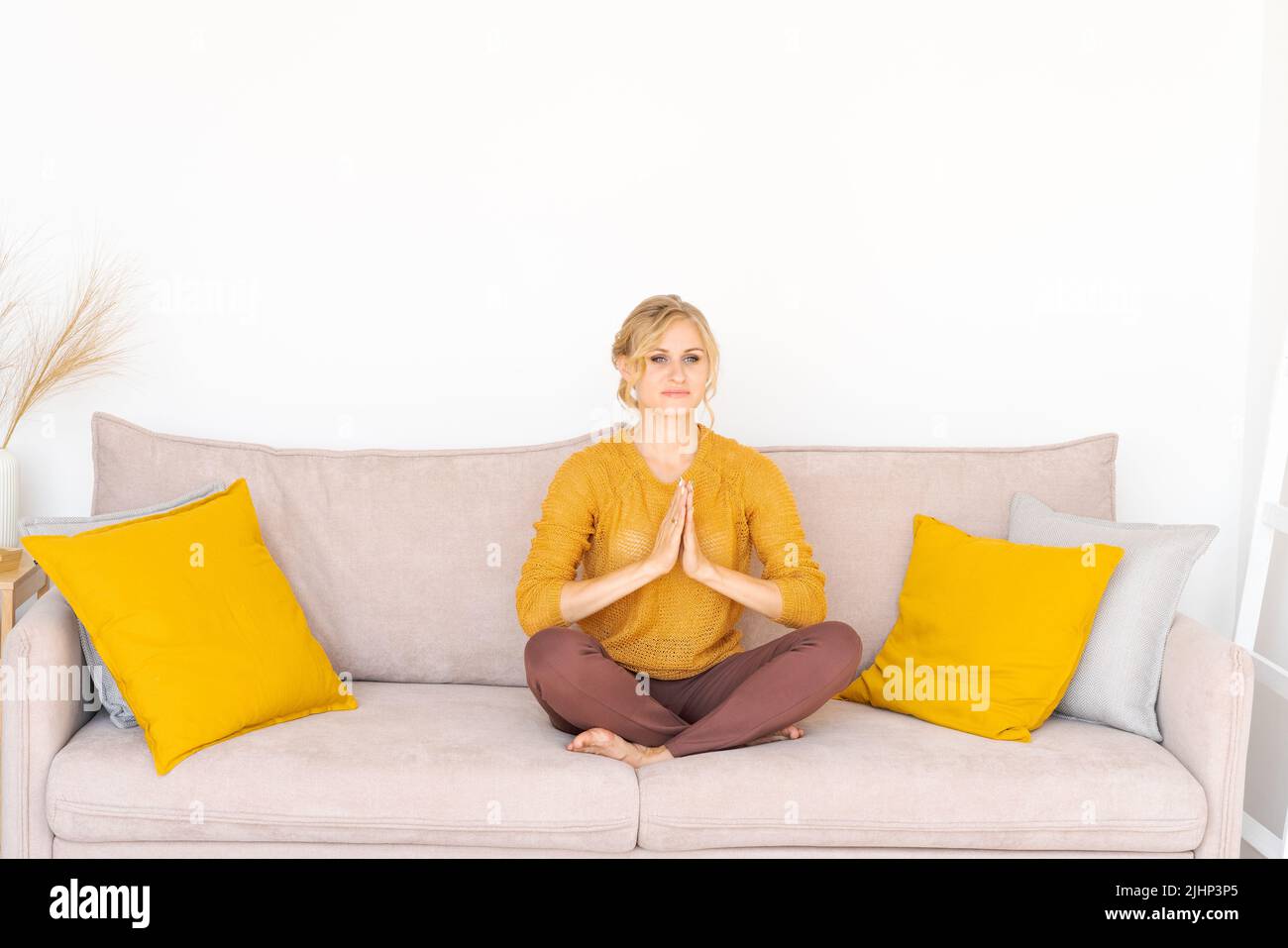 Calm caucasian woman sitting on sofa in living room, practicing yoga ...