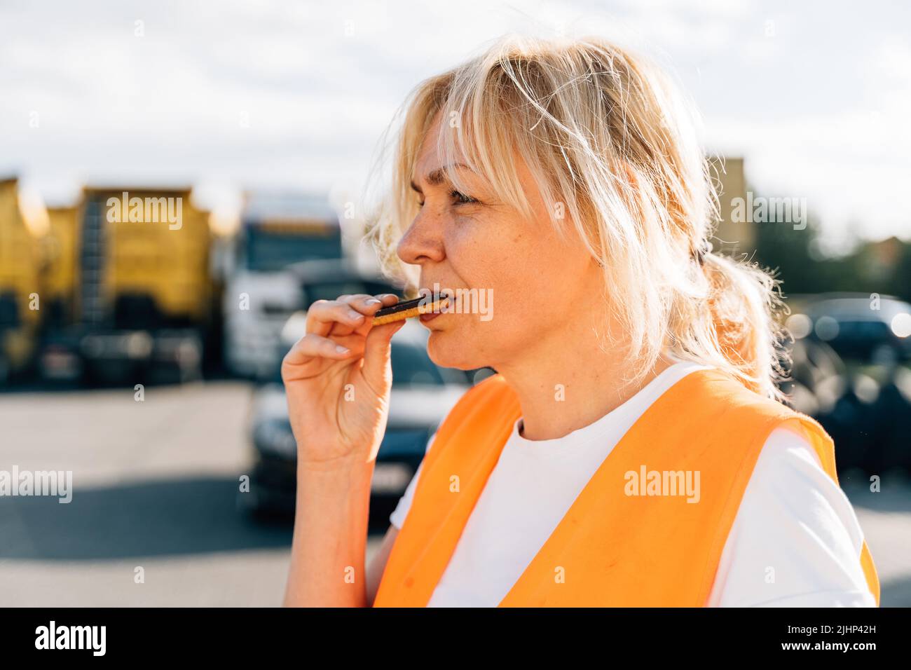 Middle aged portrait of worker engineer woman with orange vest eating ...