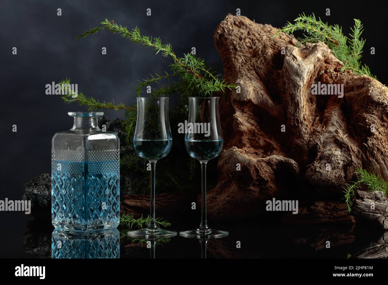 Blue gin on a black reflective background. Juniper branches, stone and ...