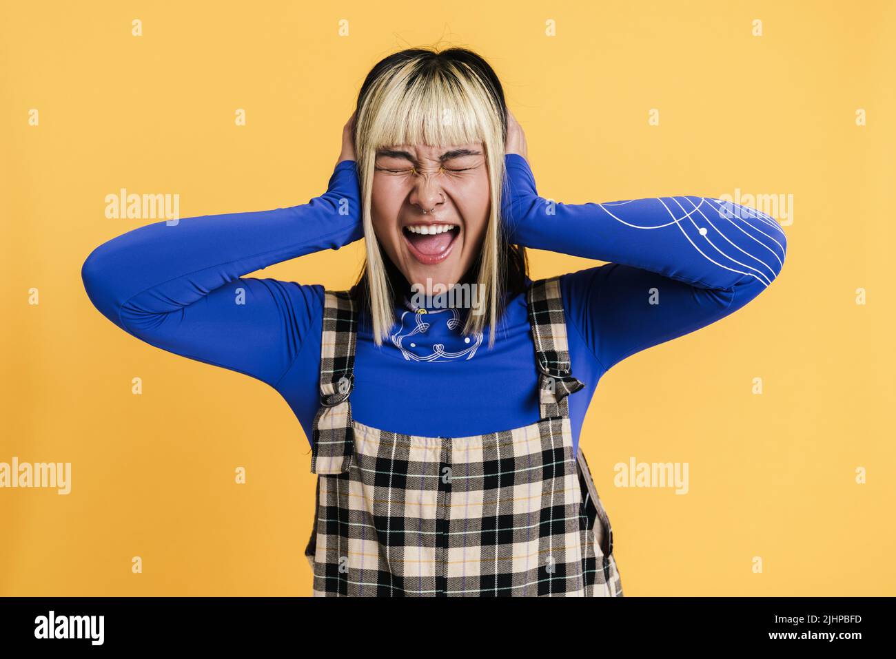 Asian girl with piercing screaming while covering her ears isolated ...