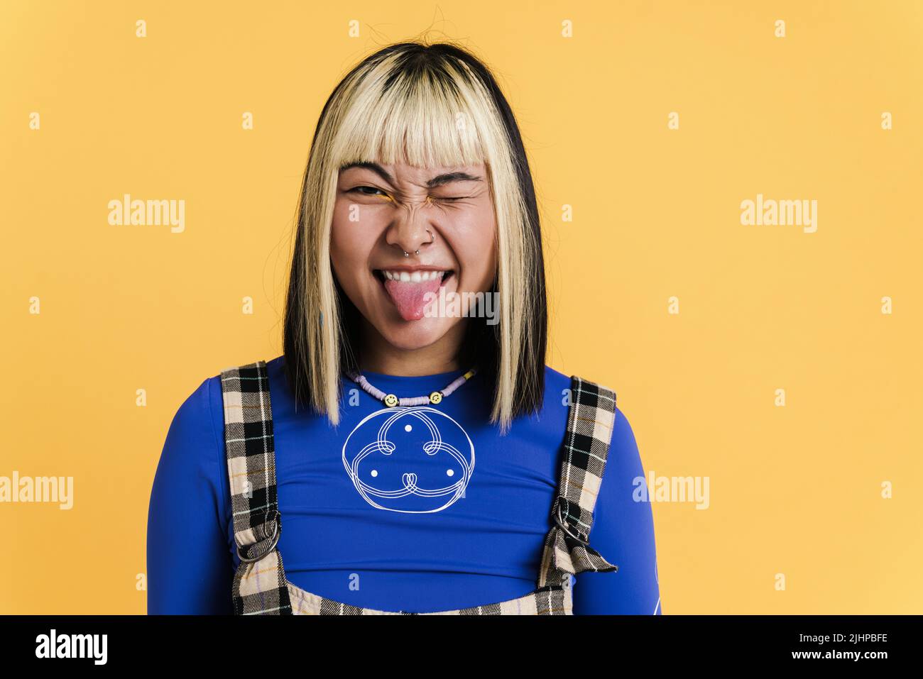 Asian Girl With Piercing Showing Her Tongue And Winking Isolated Over