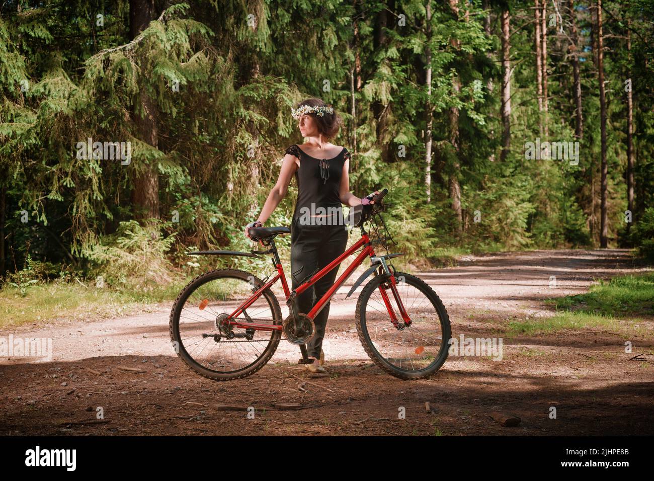 Woman in wreath of daisies with bike alone in the deep green forest ...