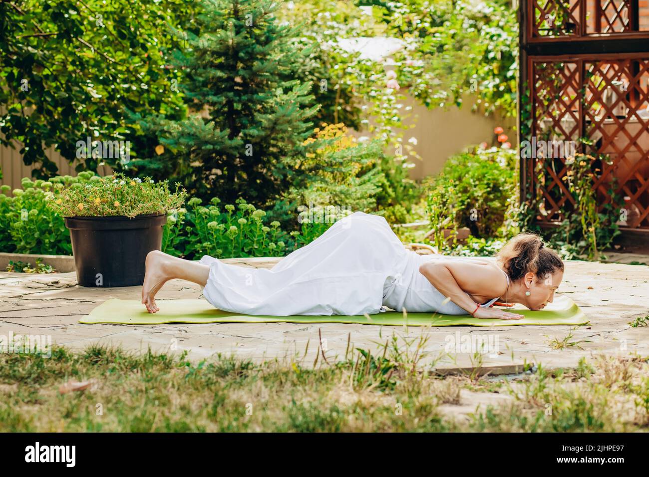 Young woman practices yoga in the garden. Surya namaskar, Four-point ...