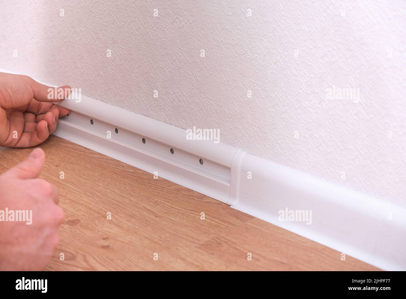 A man installs a floor skirting board. Fixing the plastic skirting ...