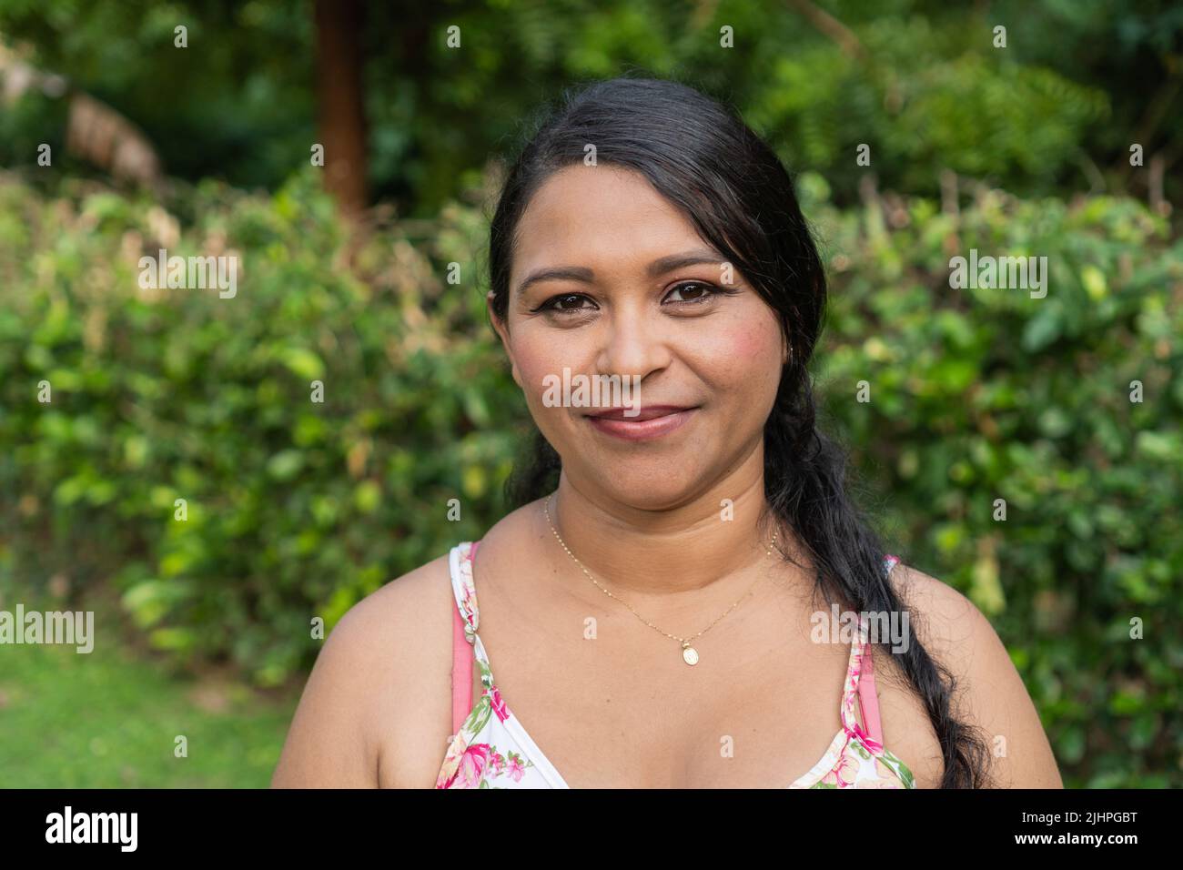 Smiling latina woman in dress standing in park Stock Photo - Alamy