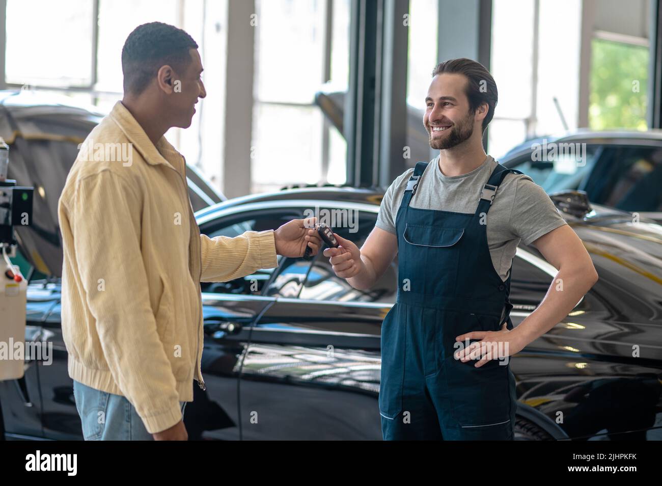 Mechanic taking car key from dark-skinned man Stock Photo - Alamy
