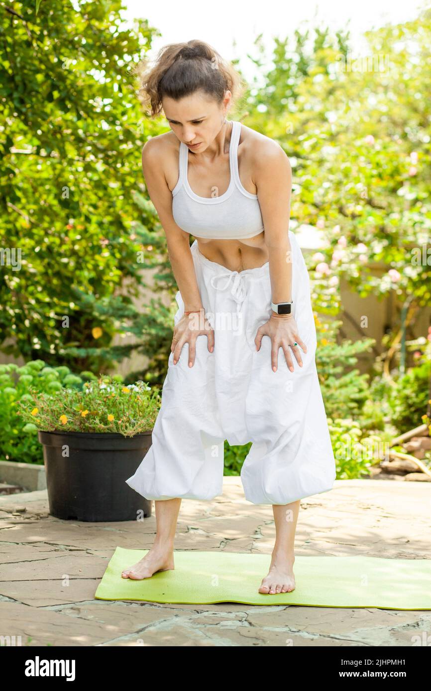 Young woman practices yoga in the summer garden. Vacuum exercise. Nauli ...