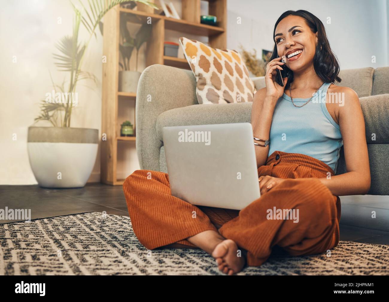 .Beautiful mixed race woman using blogging laptop and cellphone to talk to clients in home ...