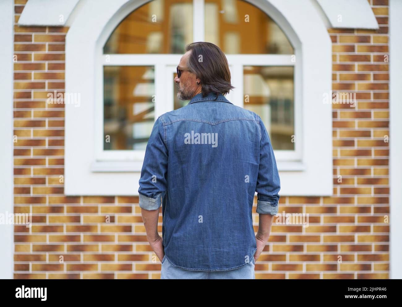 Back view of a man standing alone looking sideways at old town building ...