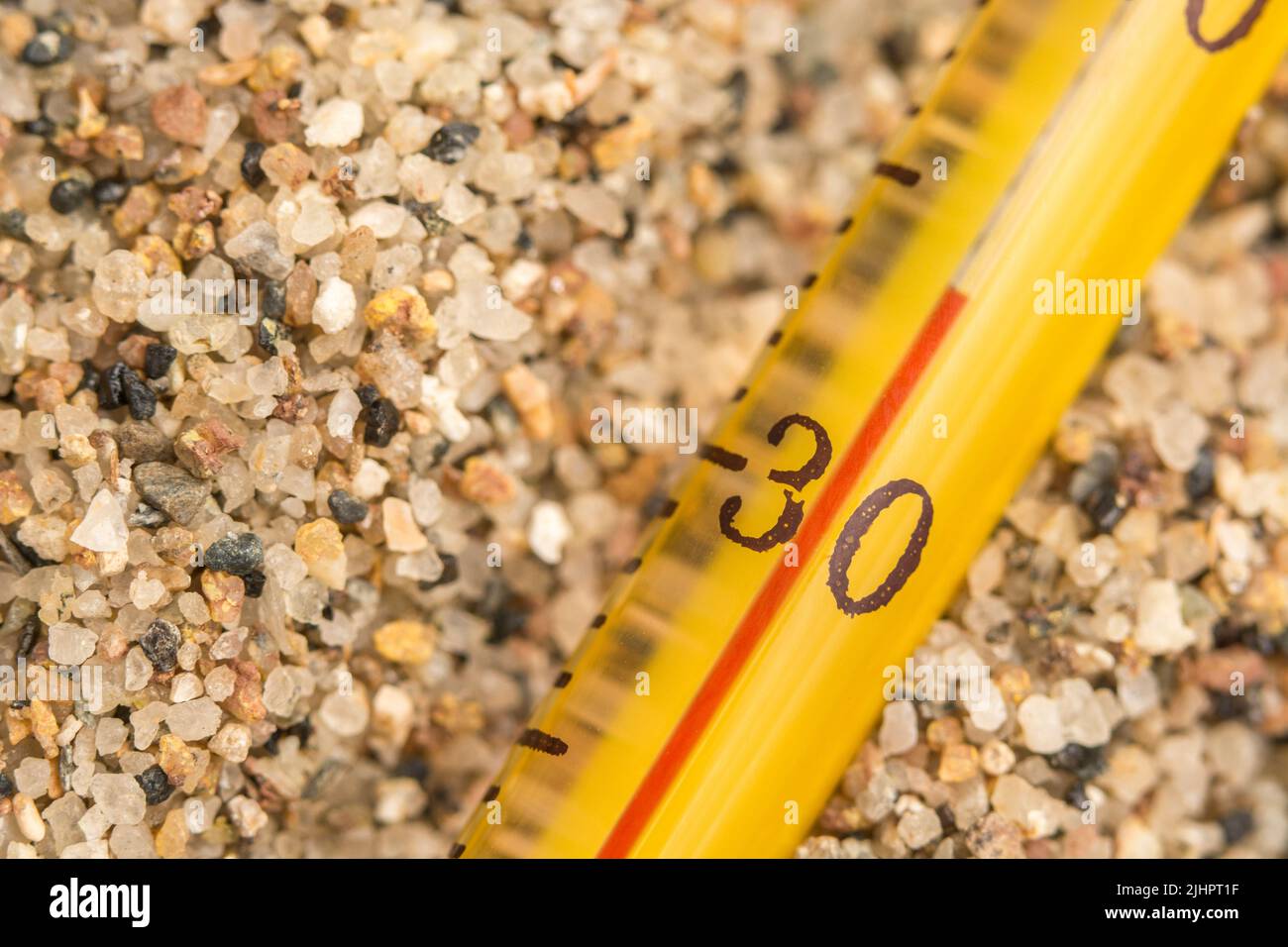 Close-up glass alcohol thermometer on coarse sand, reading 33.5 C. For ...