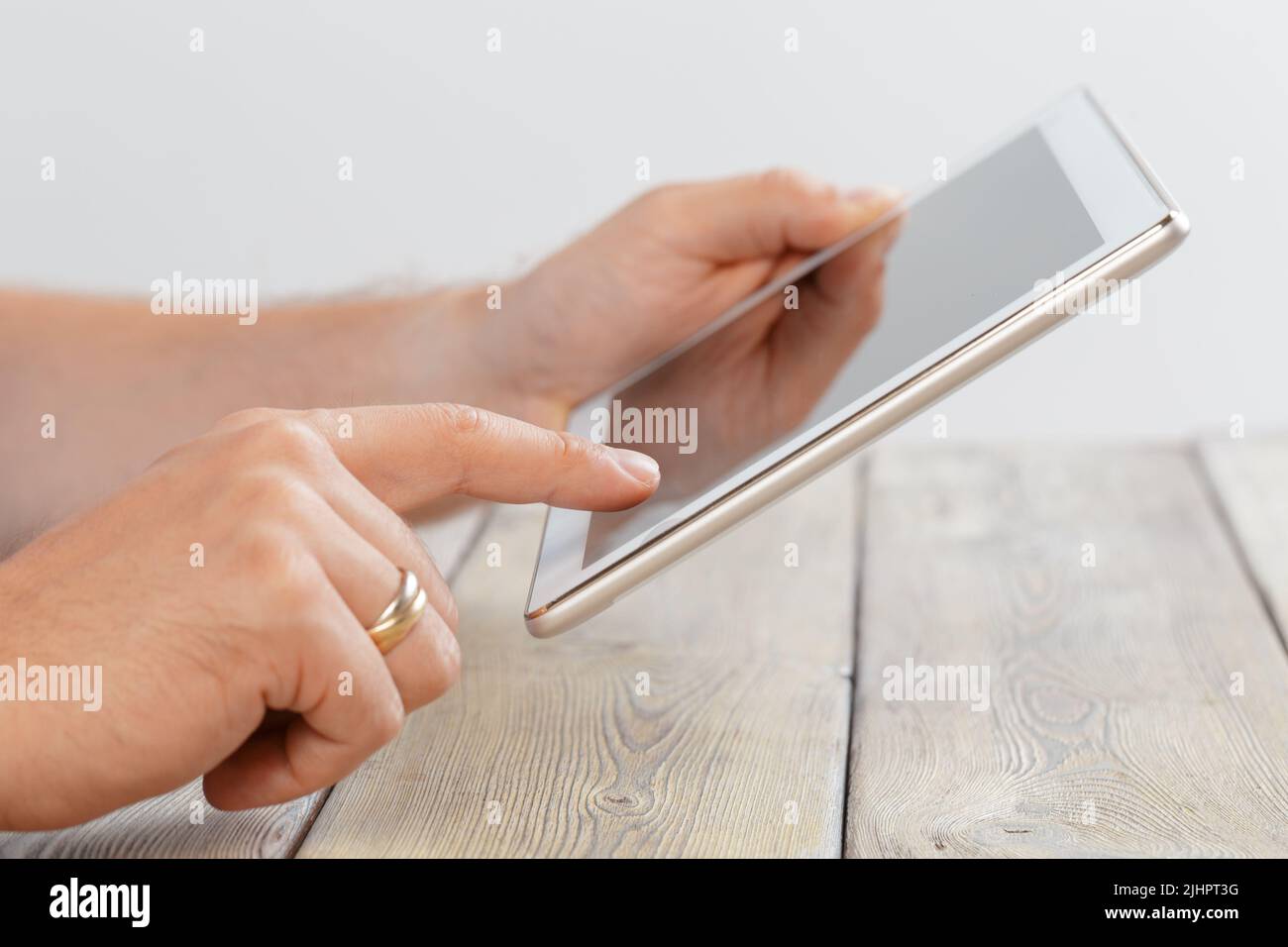 hands of a man holding tablet device over a wooden workspace table ...