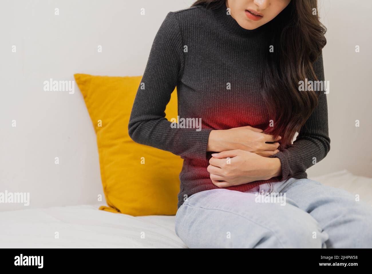 Young woman suffering from strong abdominal pain while sitting on bed ...