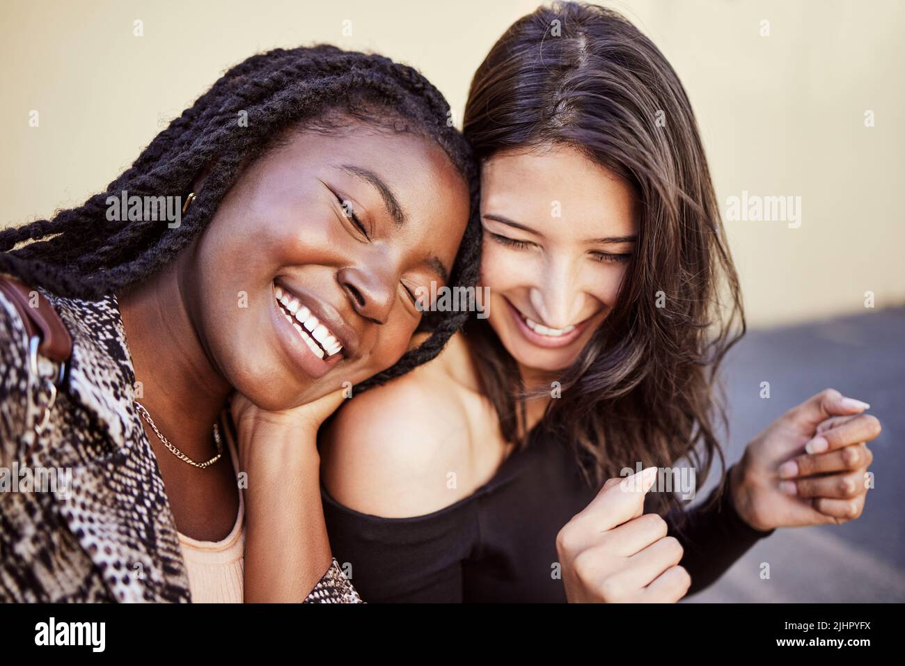 Two beautiful young female friends sitting on sidewalk spending time ...
