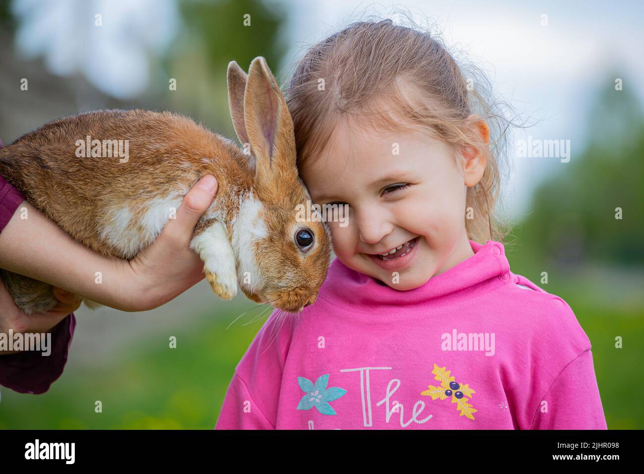 A little girl presses her cheek to a red rabbit and smiles Stock Photo ...