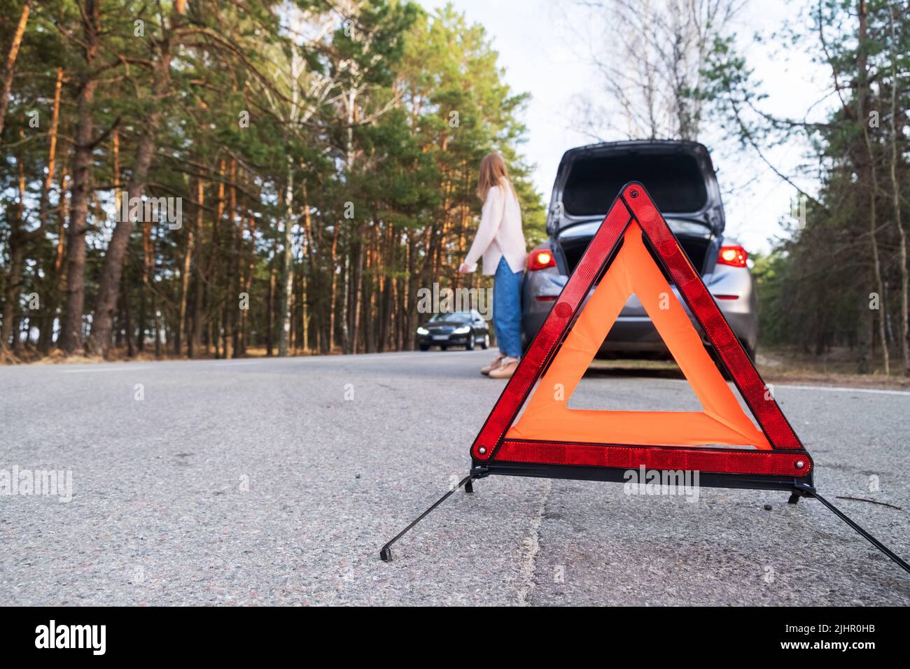 Red emergency triangle on the road amid a blurry car and a woman in ...