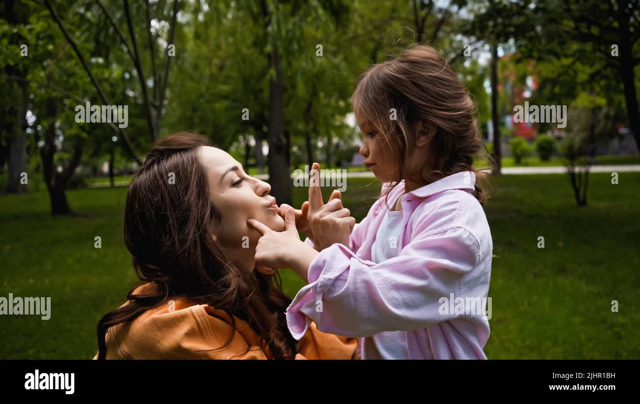happy mother pouting lips and pointing at nose of cute daughter in ...