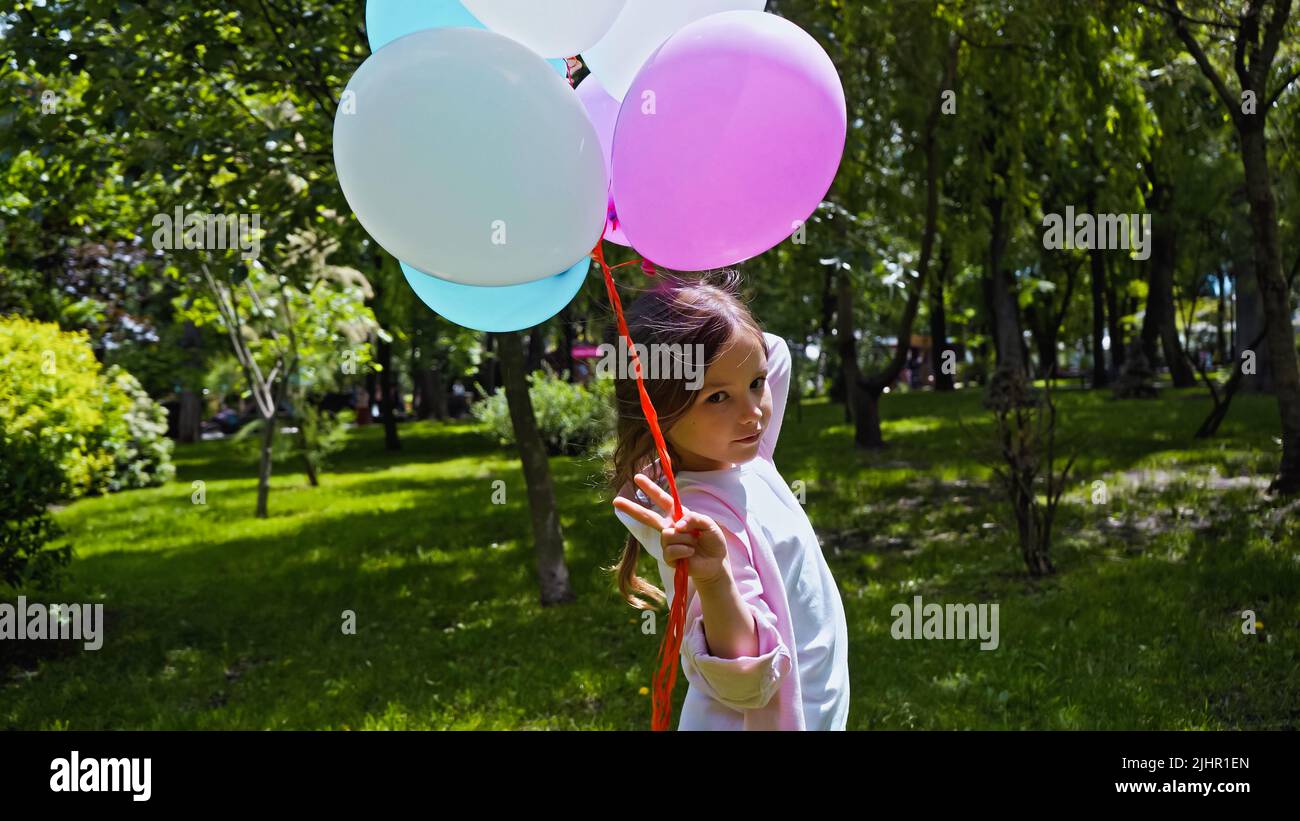 kid holding colorful balloons and showing peace sign in park Stock ...