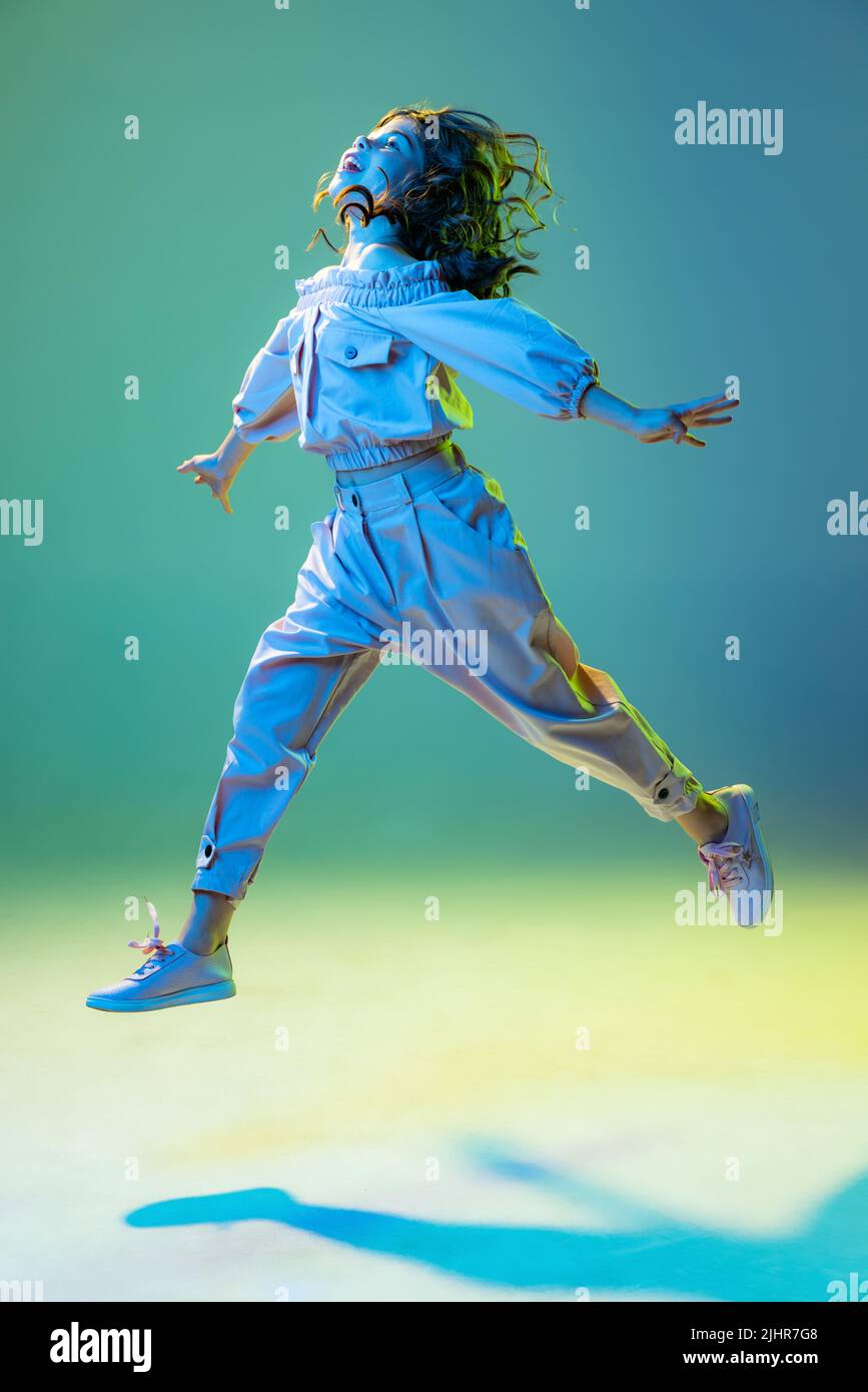 Beautiful fashionable little girl, kid posing isolated over cyan color ...