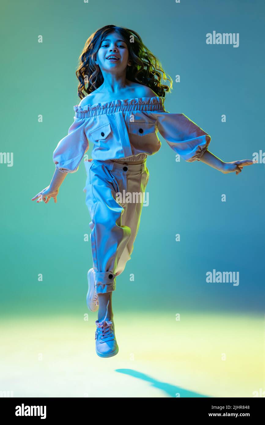 Beautiful fashionable little girl, kid posing isolated over cyan color ...