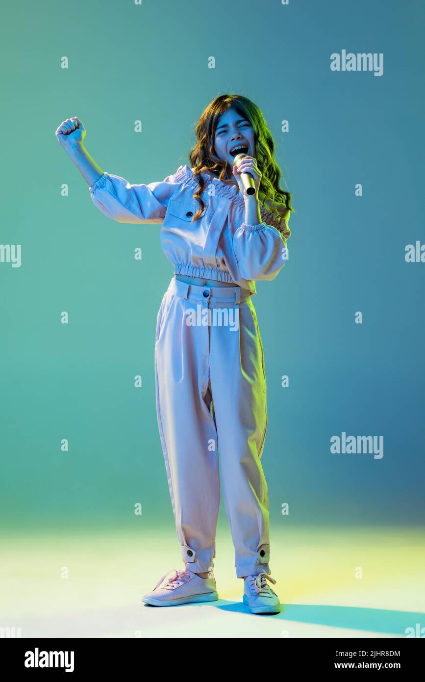 Beautiful fashionable little girl, kid singing isolated over cyan color ...