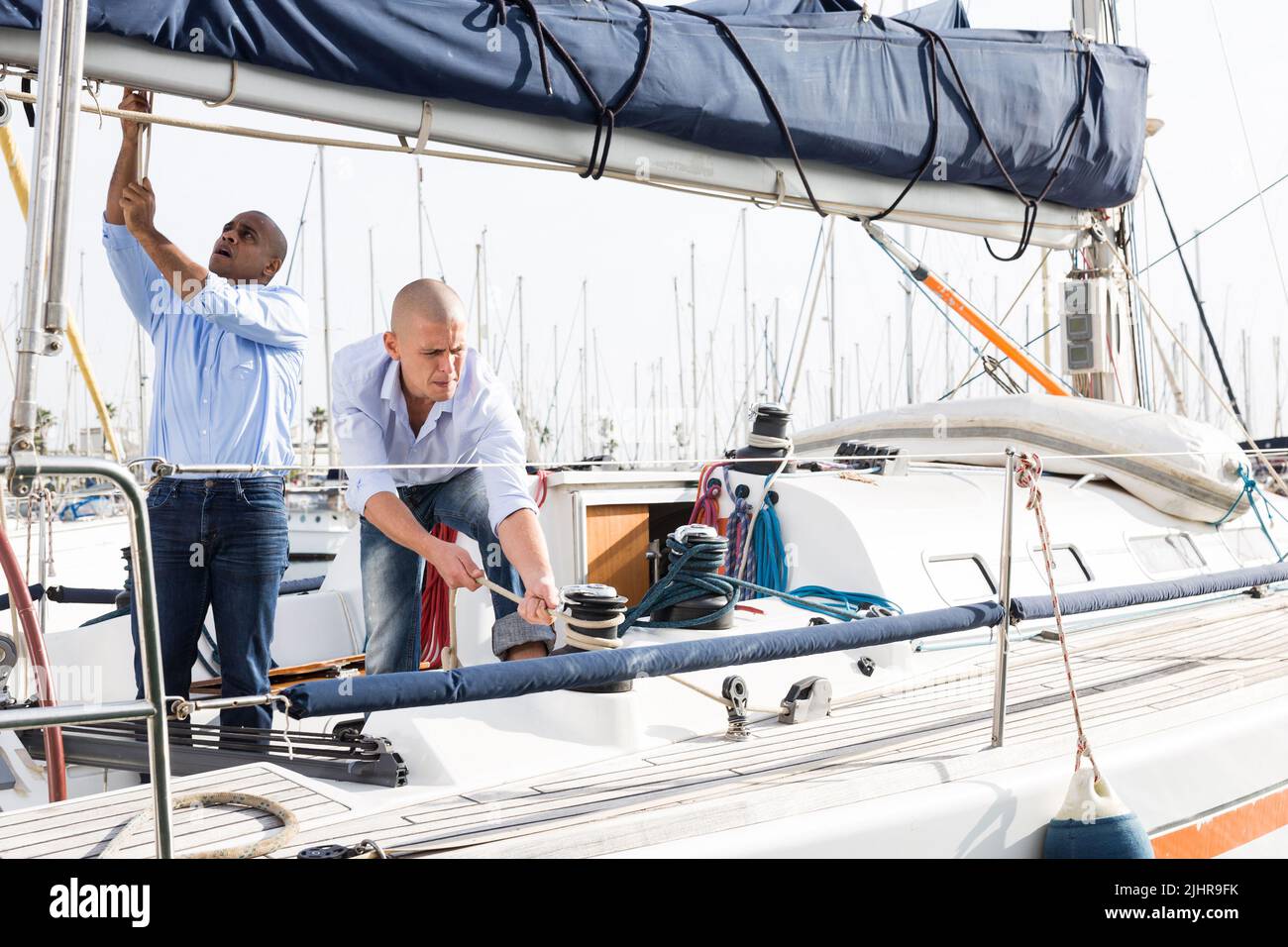 Two young men in blue shirts tidy up private sailing yacht in the ...