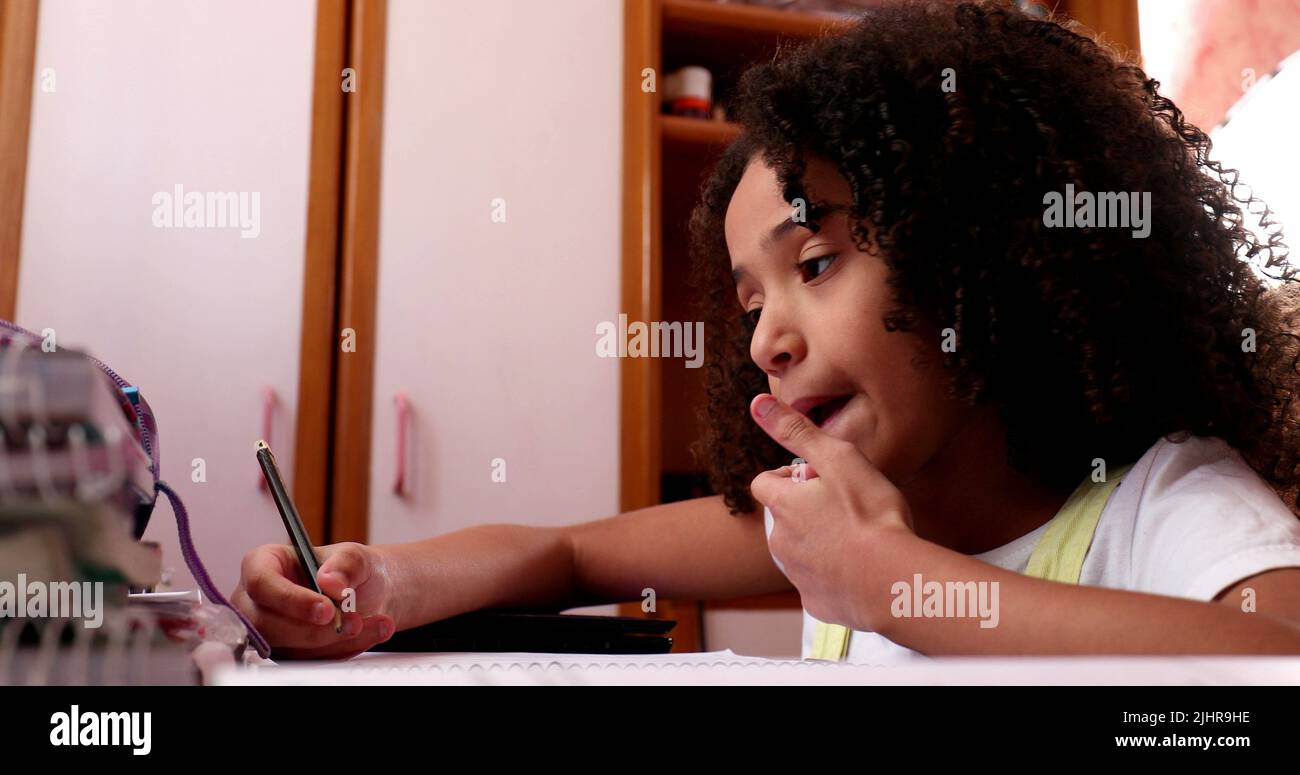 Mixed race girl writing notes doing homework at home. Little girl kid ...