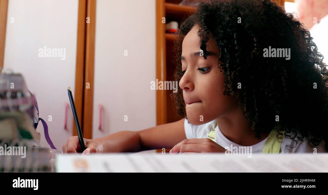 Mixed race girl writing notes doing homework at home. Little girl kid ...