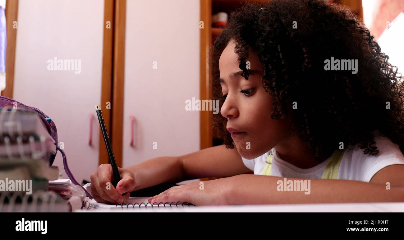 Mixed race girl writing notes doing homework at home. Little girl kid ...