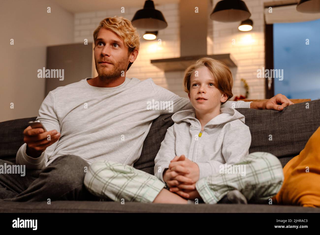 Ginger son and father watching TV while sitting on sofa together at ...