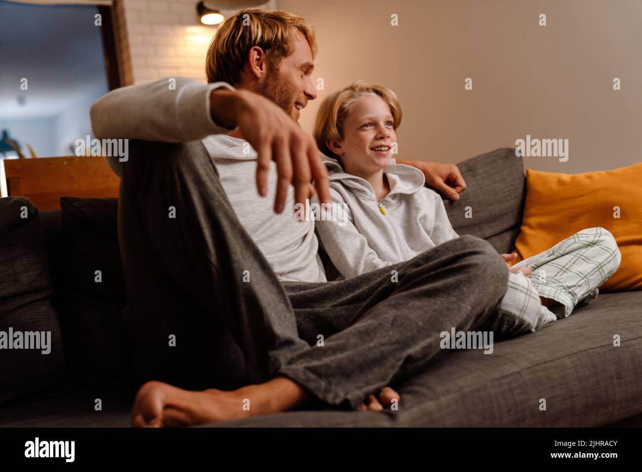 Ginger son and father laughing while sitting on sofa together at home ...