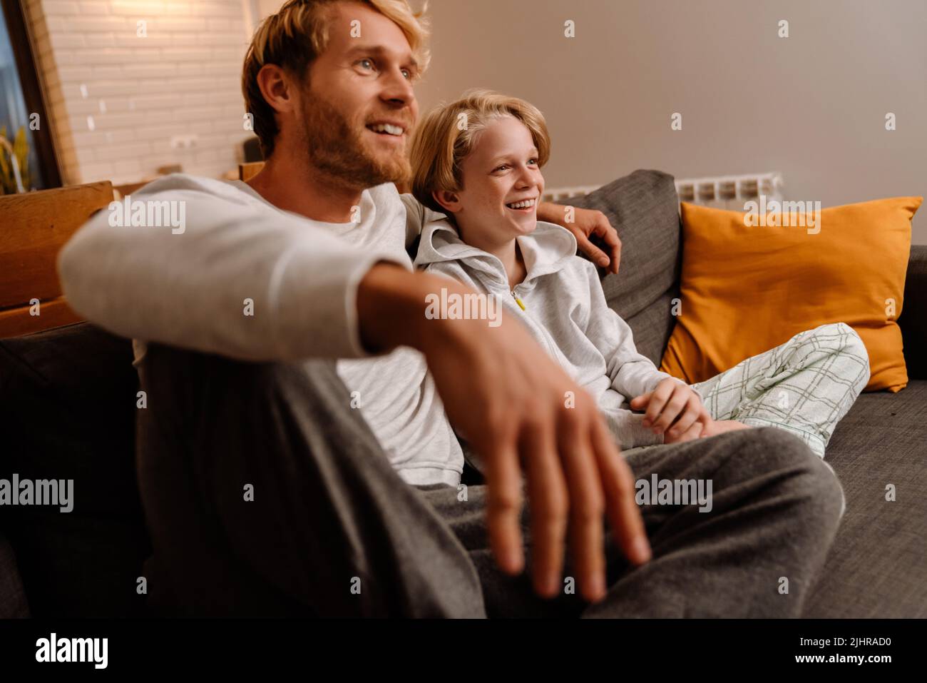 Ginger son and father laughing while sitting on sofa together at home ...