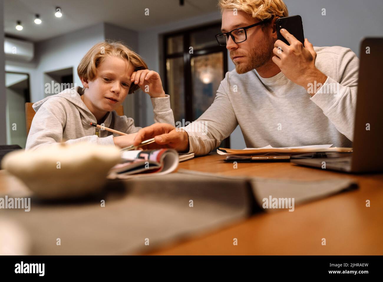 Ginger son doing homework with his father while sitting at desk in home ...