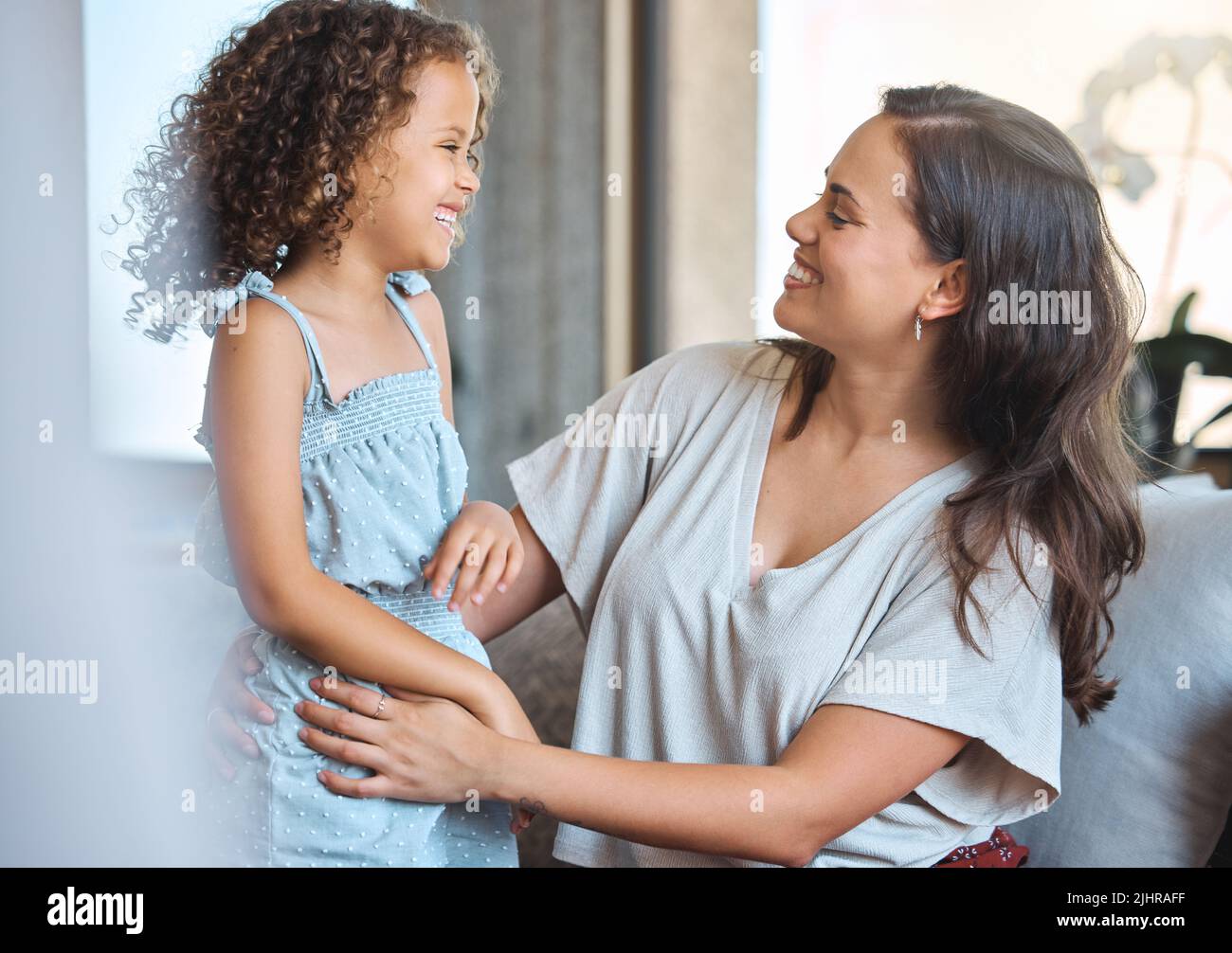 Adorable little girl and loving mother talking and laughing while spending time together at home ...