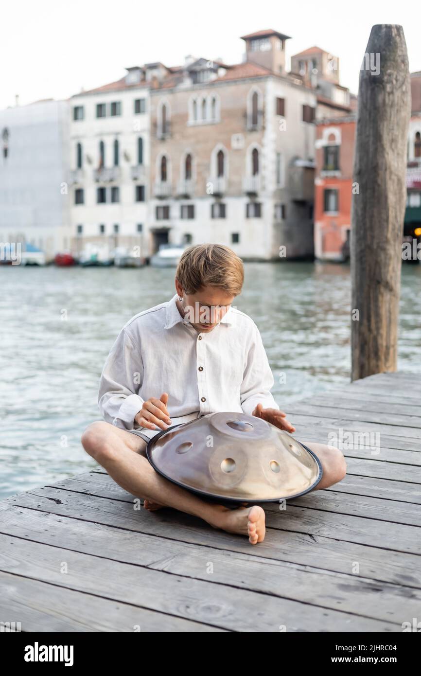 Barefoot musician playing hang drum on pier near river in Venice Stock ...