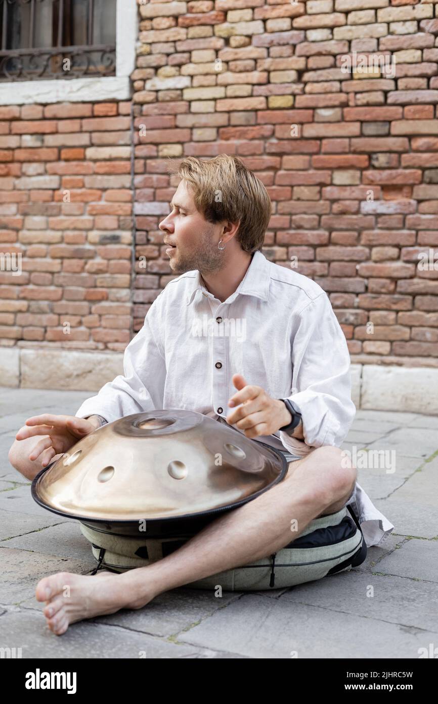 Side view of barefoot musician performing handpan on urban street in ...