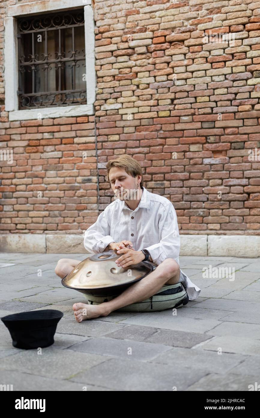 Barefoot musician with closed eyes playing handpan on urban street in ...