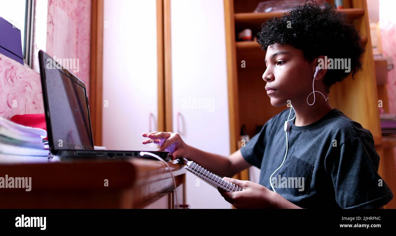 Teen boy studying at home in front of laptop computer. Mixed race kid ...
