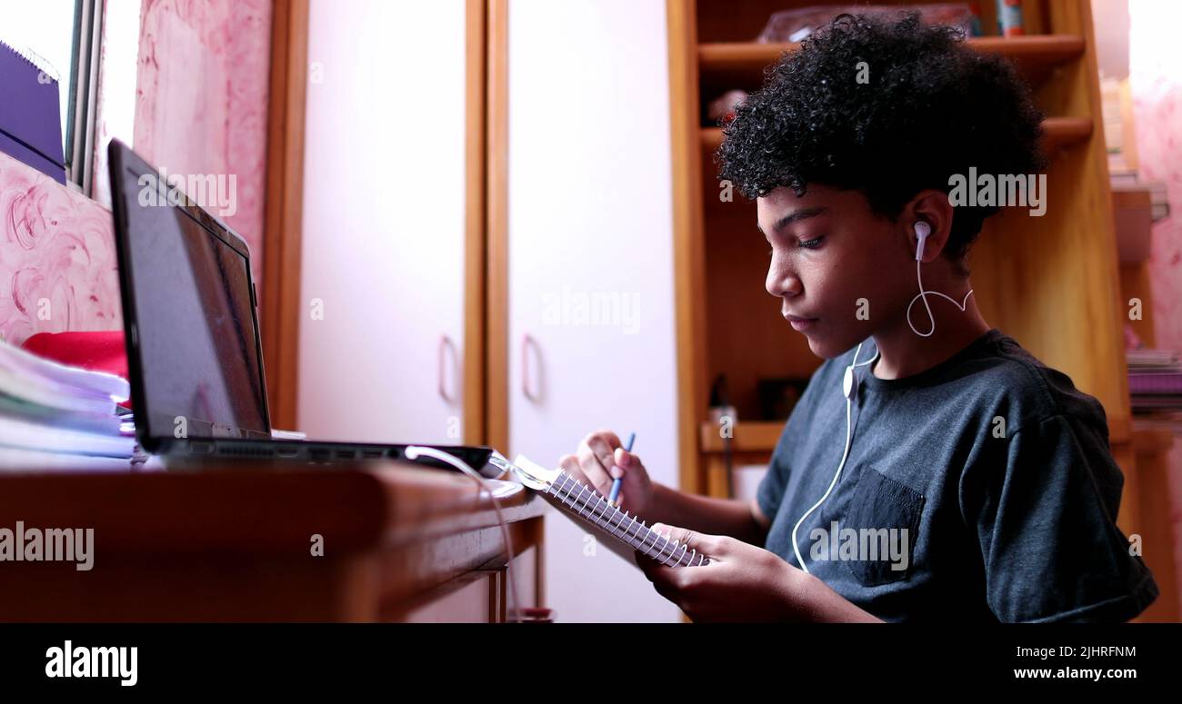 Teen boy studying at home in front of laptop computer. Mixed race kid ...