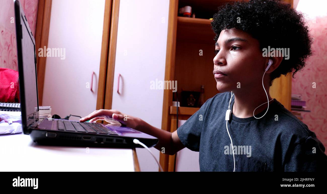 Teen boy studying at home in front of laptop computer. Mixed race kid ...
